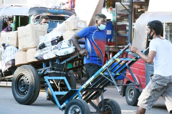 A worker pulling a hand-cart laden with goods